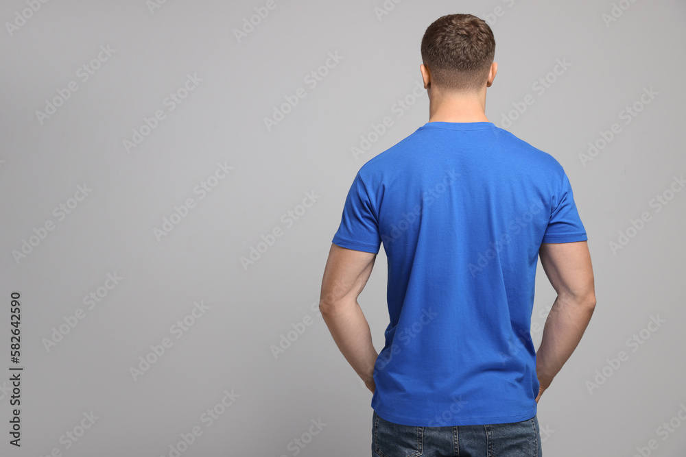 Man wearing blue t-shirt on light grey background, back view. Mockup ...