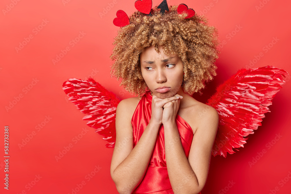 Sad female cupid keeps hands under chin looks displeased wears dress ...