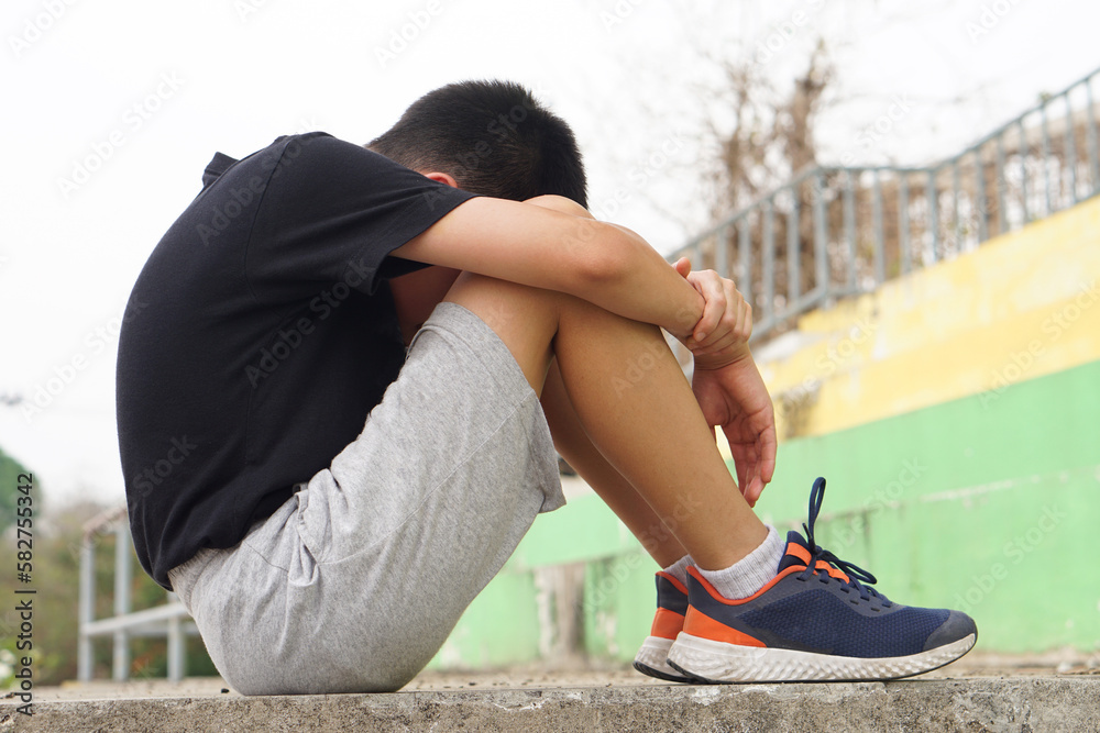 Depressed unidentified boy sits alone outdoor, sad and cry, face down ...