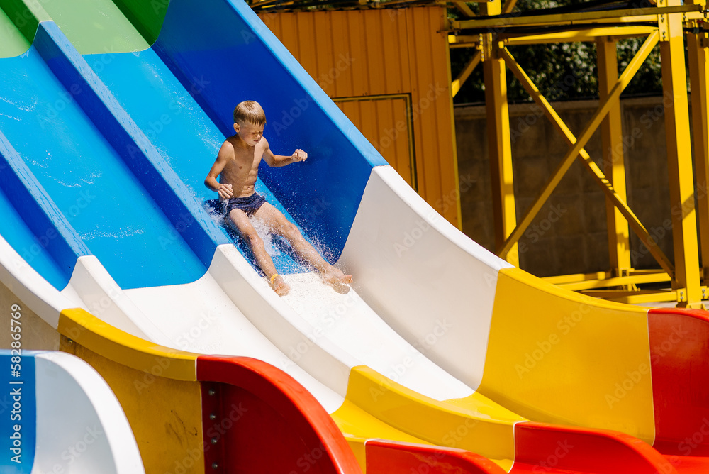 A little boy slides down a water slide and has fun. The boy swims in ...