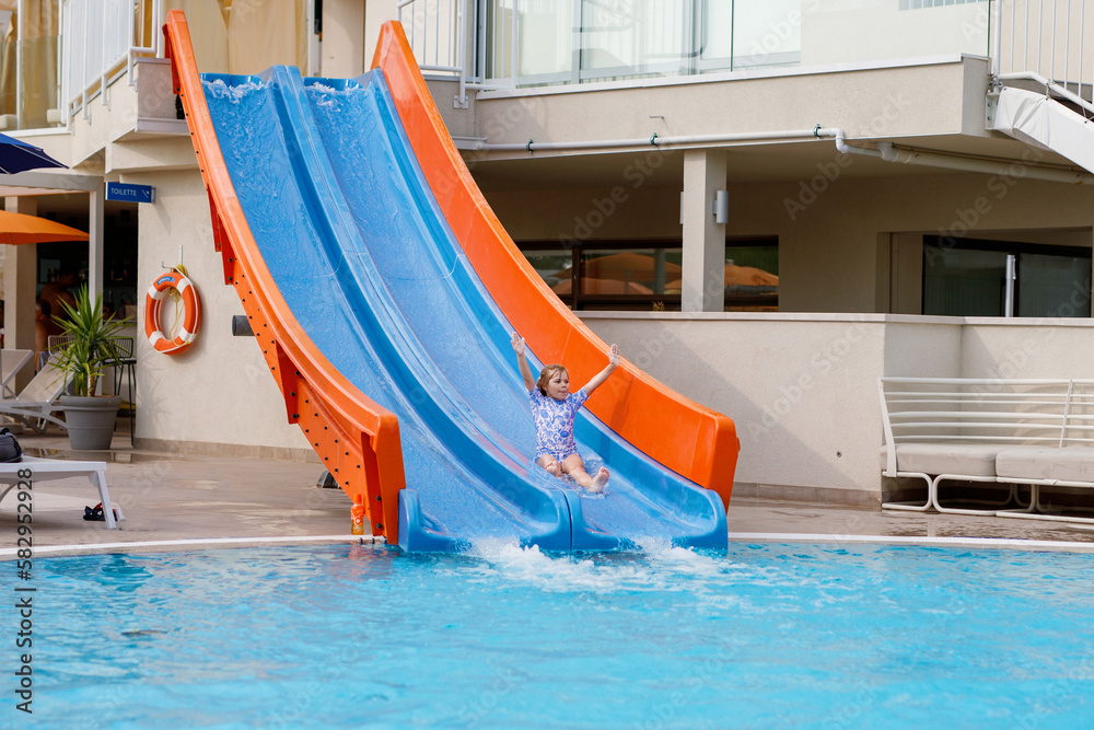 Little preschool girl sliding on a children slide in outdoor swimming ...