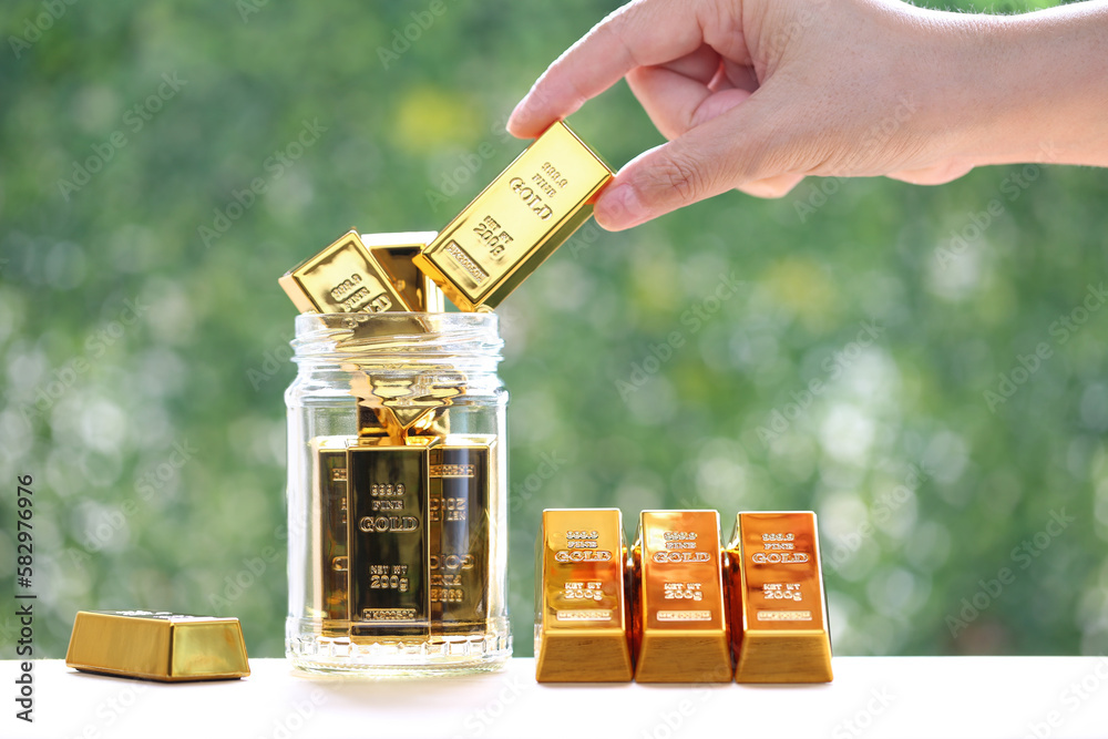Saving gold, Woman hand putting gold bar in the glass bottle on natural ...