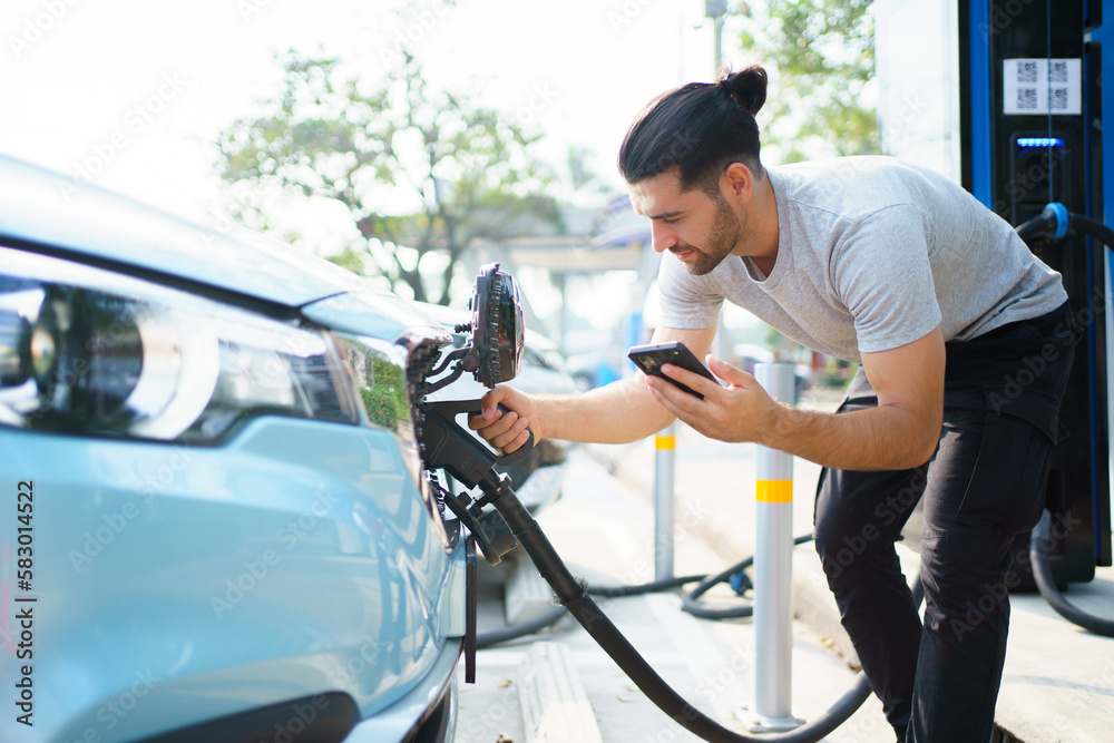 Handsome Asian young man holding an EV plug connector and attaching ...