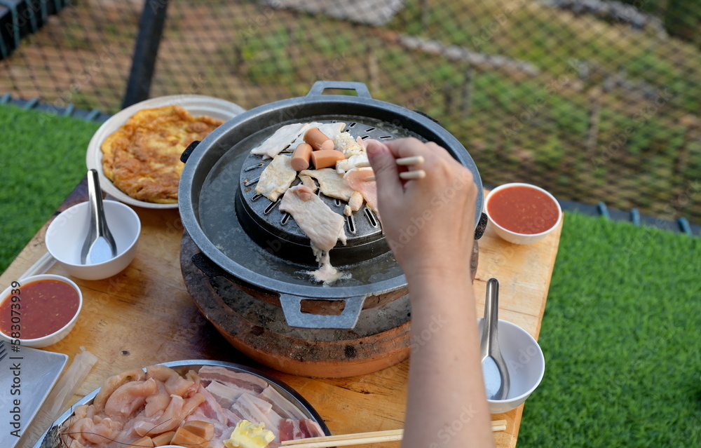 Right hand uses chopsticks to pick up pork, beef, seafood to be grilled ...