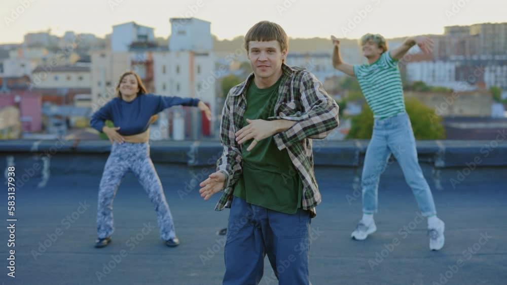 Three people dancing on the roof looking at camera. Young man dancing ...