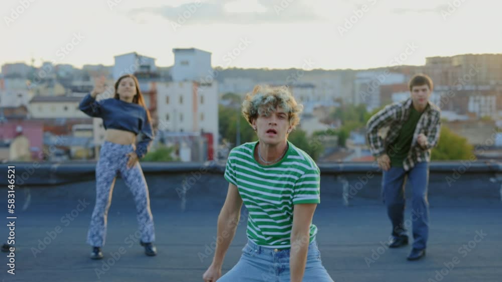 Three people dancing on the roof looking at camera. Young man dancing ...