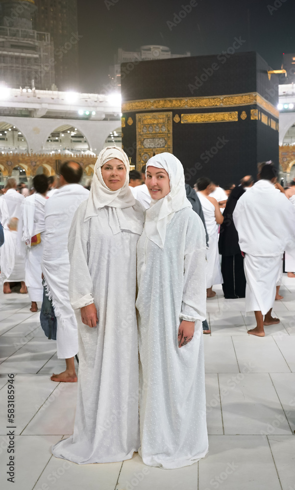Two caucasian women in long white dress standing in front of the Kaaba ...
