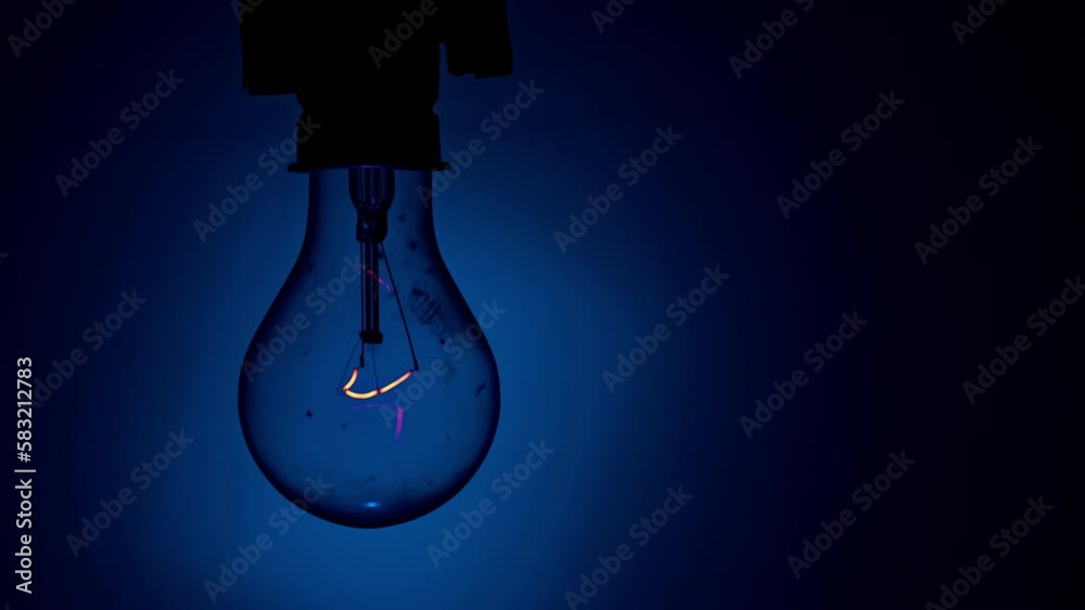 Stockvideon Light bulb lights up on a blue background in the dark. Slow ...