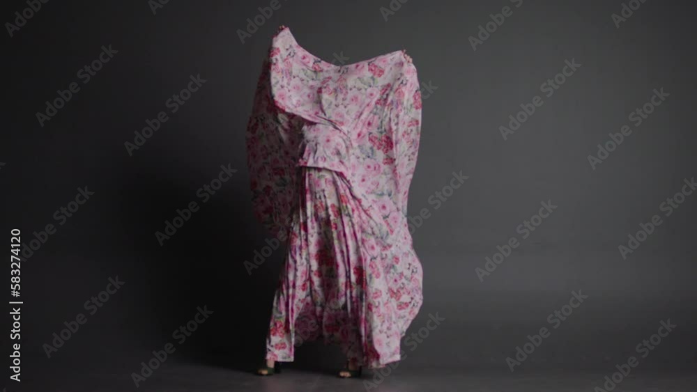 A girl in a long colored dress with flowers on which a strong wind ...