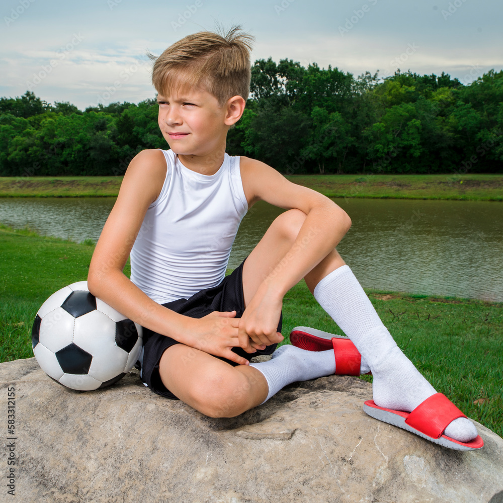 Young preteen boy sitting on rock with soccer ball outside Stock Photo ...