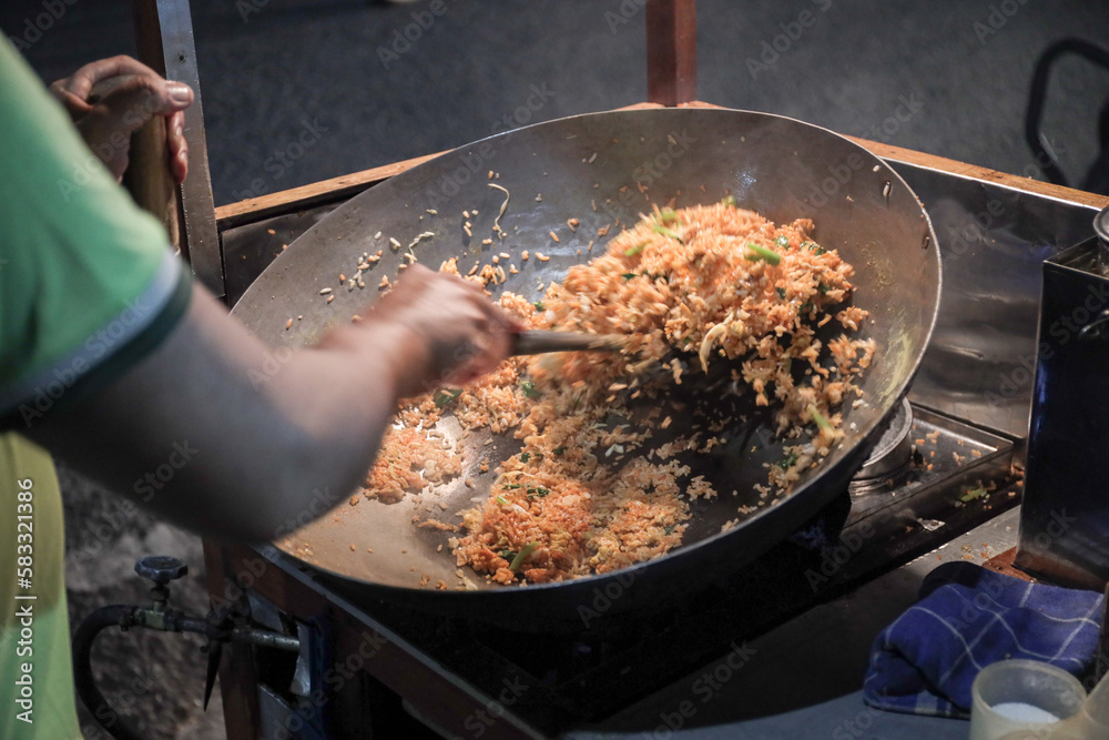 A man cooking fried rice on steel skillet pan for selling on the street ...