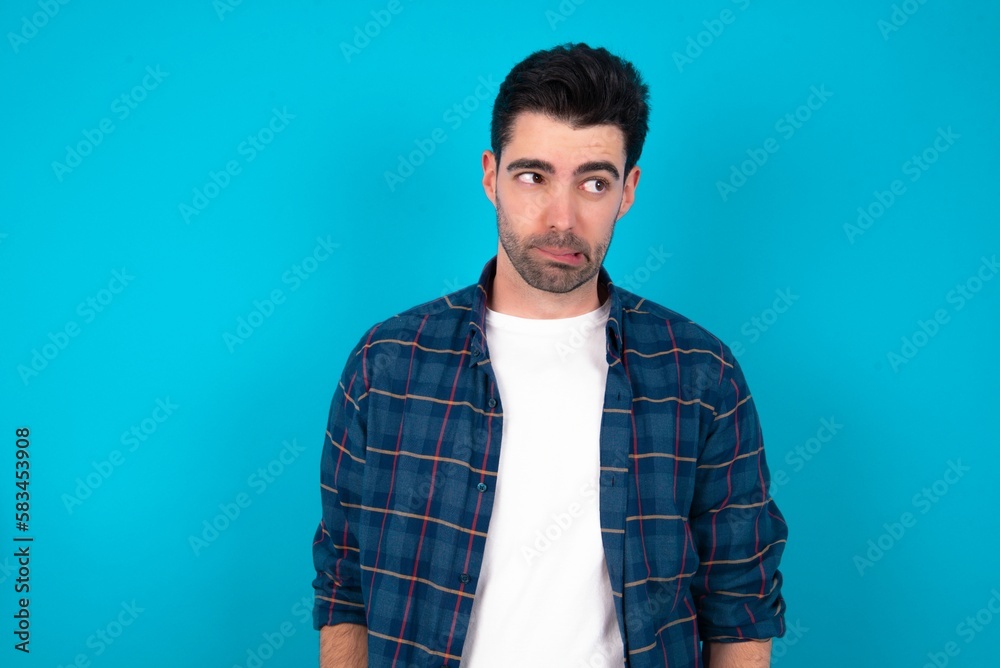 Young man standing over blue studio background making grimace and crazy ...