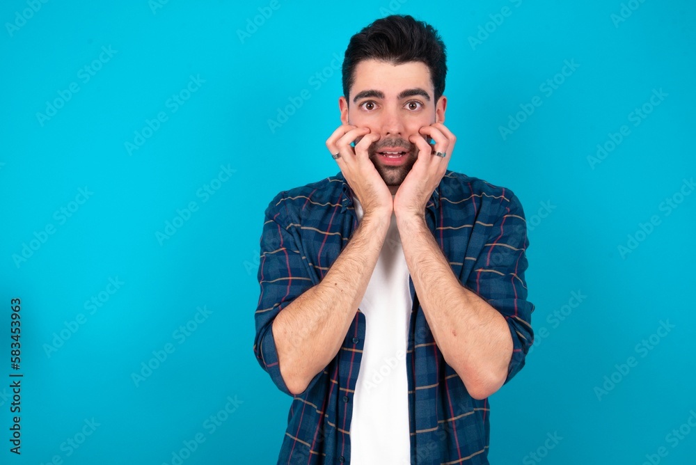 Stupefied Young man standing over blue studio background expresses ...