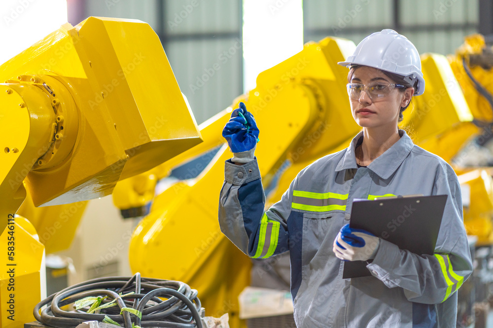 Female engineer wearing uniform and safety helmet inspects the robot ...