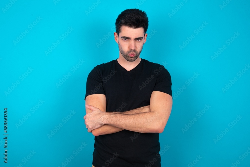 Gloomy dissatisfied Young man wearing black T-shirt over blue studio ...