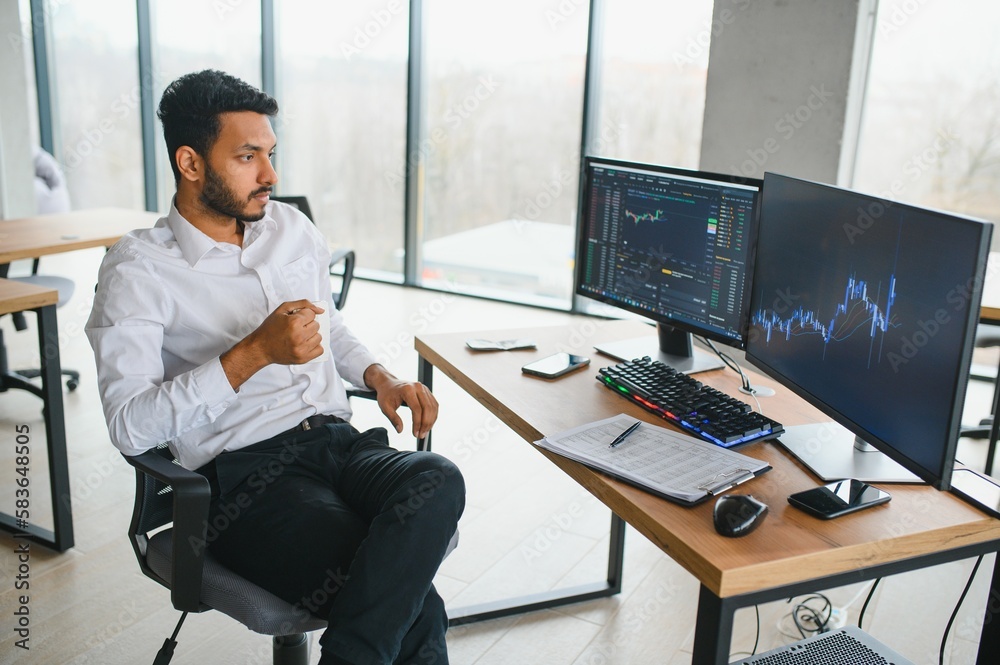 Side view of smart Indian crypto trader, investor, analyst broker, using laptop and smartphone ...