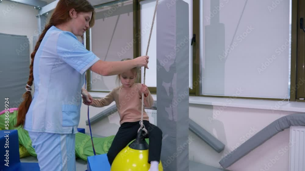Child with physiotherapist on swing in sensory integration room. Little ...