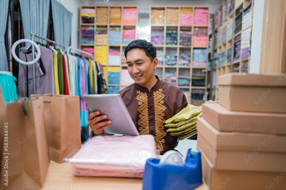 happy male seller using tablet while sitting on a desk with his product ...