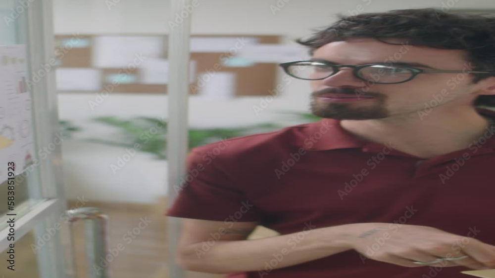 Vertical shot of young man pointing at sticky notes attached to glass ...