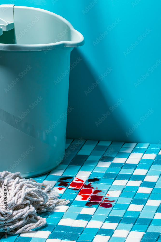Plastic container and floor mop with blood stains on tiled surface ...