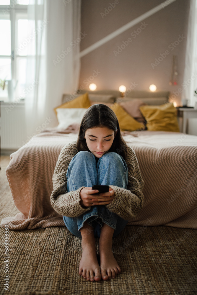 Teenage girl sitting on the floor and scrolling her smartphone. Stock Photo | Adobe Stock