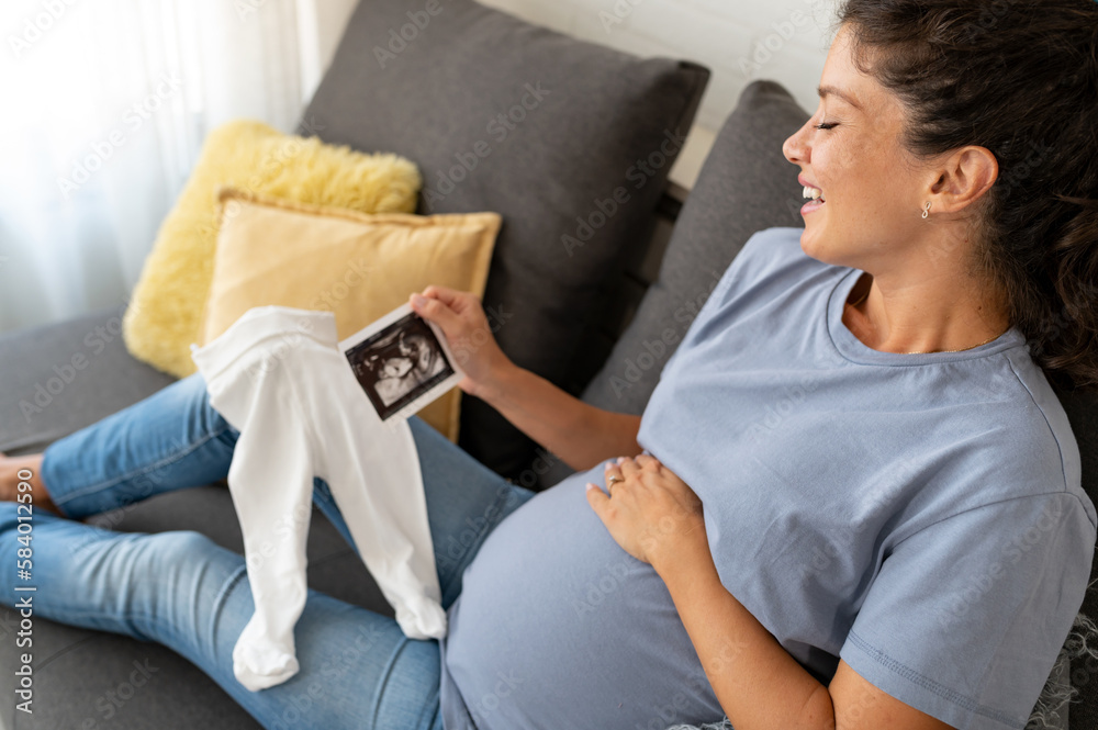 Beautiful pregnant woman looking a cute baby clothes and ultrasound ...