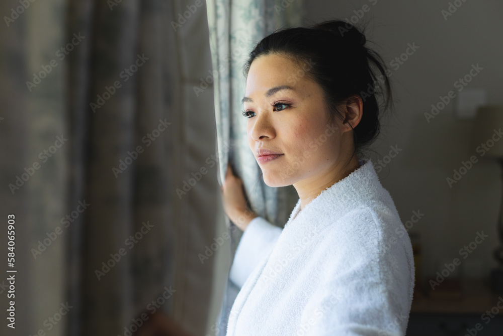Happy asian woman wearing bathrobe, opening curtain and looking through ...