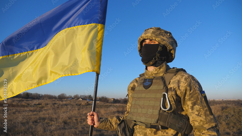 Male soldier in military uniform and helmet holds a waving flag of ...