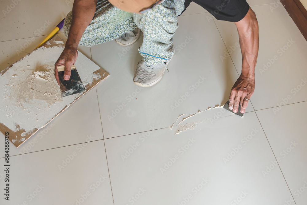 A handy man applies grout to fill the gaps of white porcelain floor ...