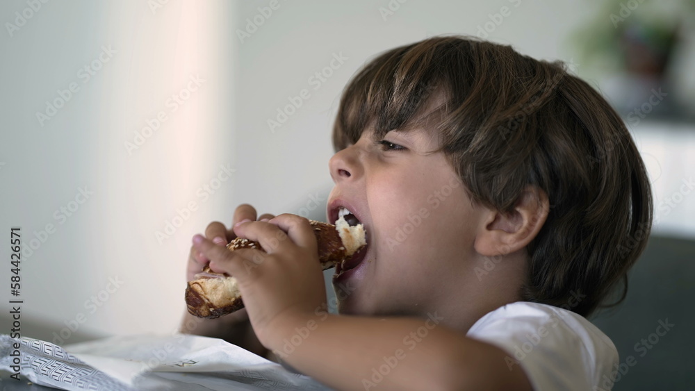 One little boy grabbing bread taking a bite of carb food seated at ...