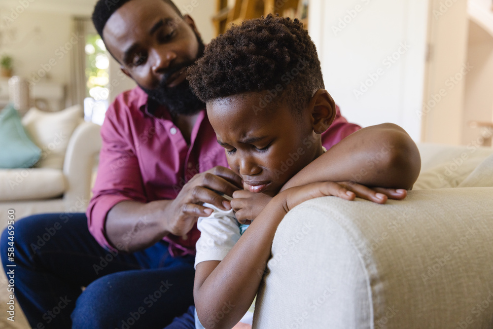 African american father sitting on sofa in living room, cheering up his ...