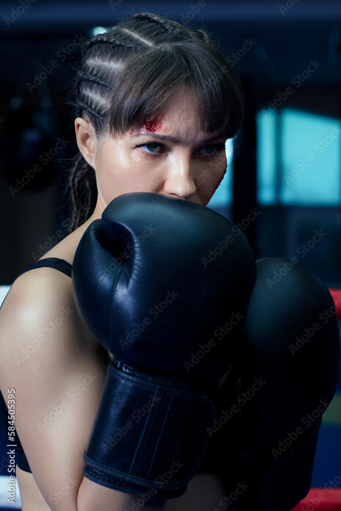 Female fighter with boxing gloves on her hands stands in a boxing ring ...