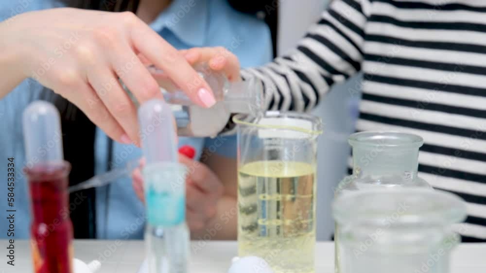 Young woman mixing liquids in test tube with multiethnic children ...