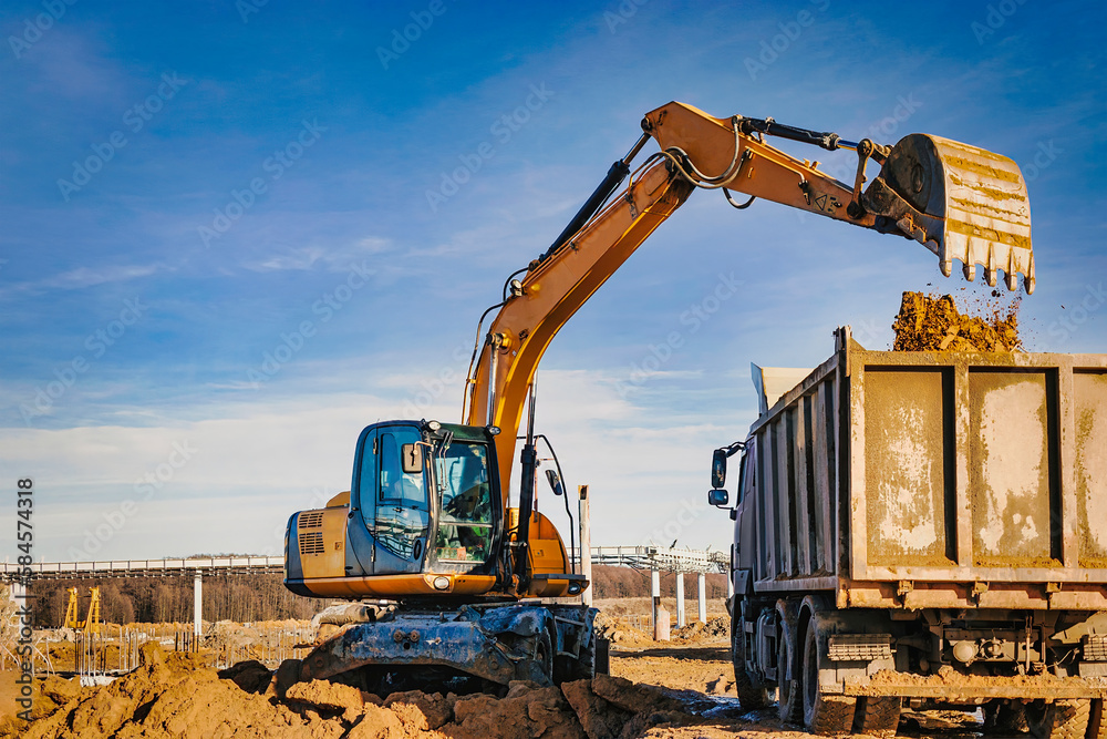 A wheeled excavator loads a dump truck with soil and sand. An excavator ...
