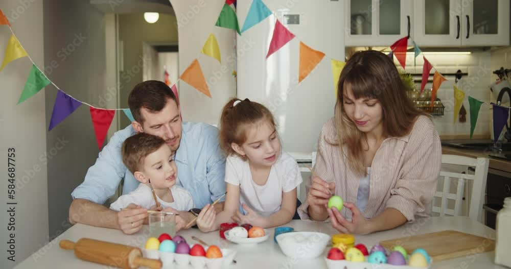Joyful family of four painting Easter eggs together at the table in ...