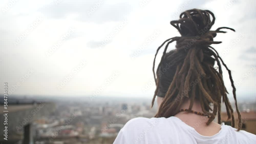 A look from behind a young guy with dreadlocks and beads around his ...