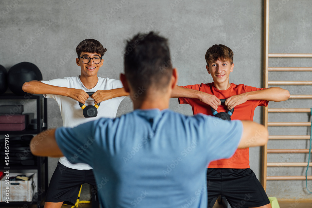 Back view of fitness instructor teaching boys kettle bell class in dark ...