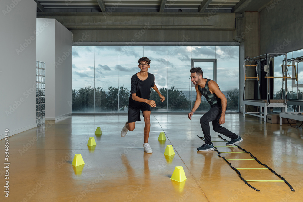 Full length of personal trainer encouraging boy during circuit training ...