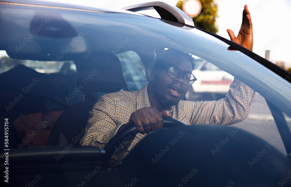 Frustrated man driving car and yelling through window with raised arm ...