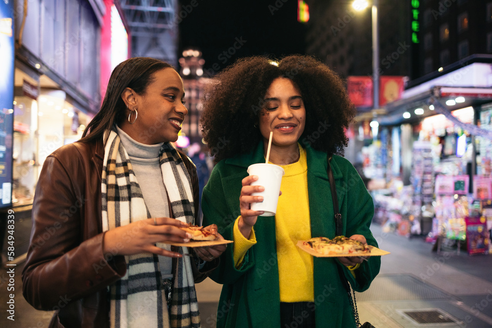 Foto de Young black women eating fast food on the street at night do ...