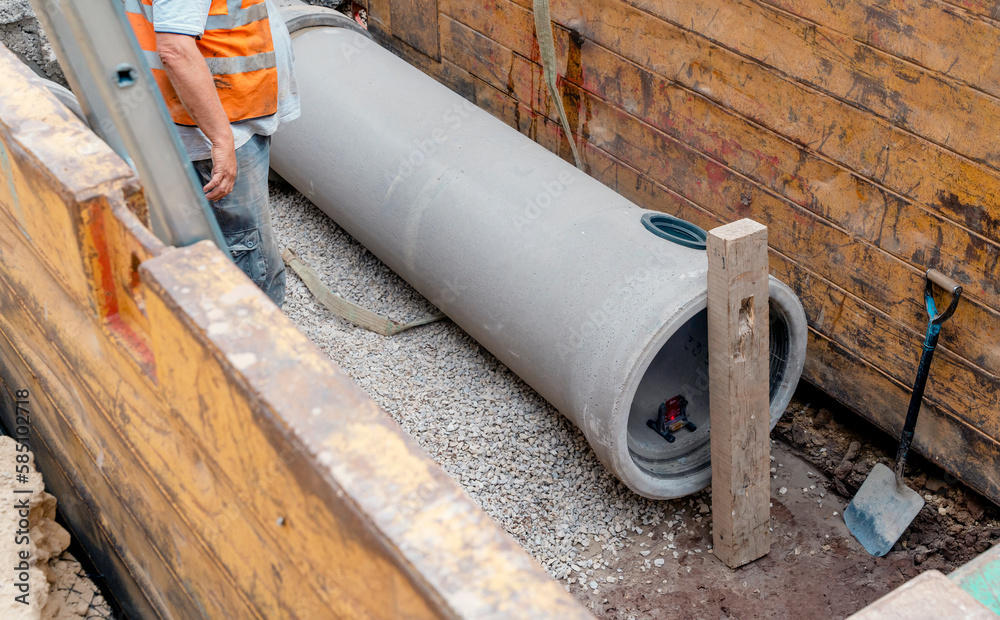 Builder installing big diameter concrete drainage pipe protected by ...