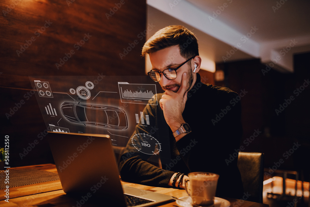 An engineer using a laptop in a cafe while viewing a hologram of the automotive industry. HUD of ...