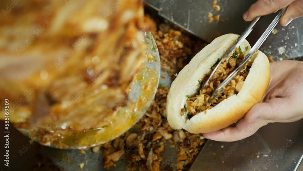Top view chef's hand holding a cut bun puts juicy pieces of fried meat ...