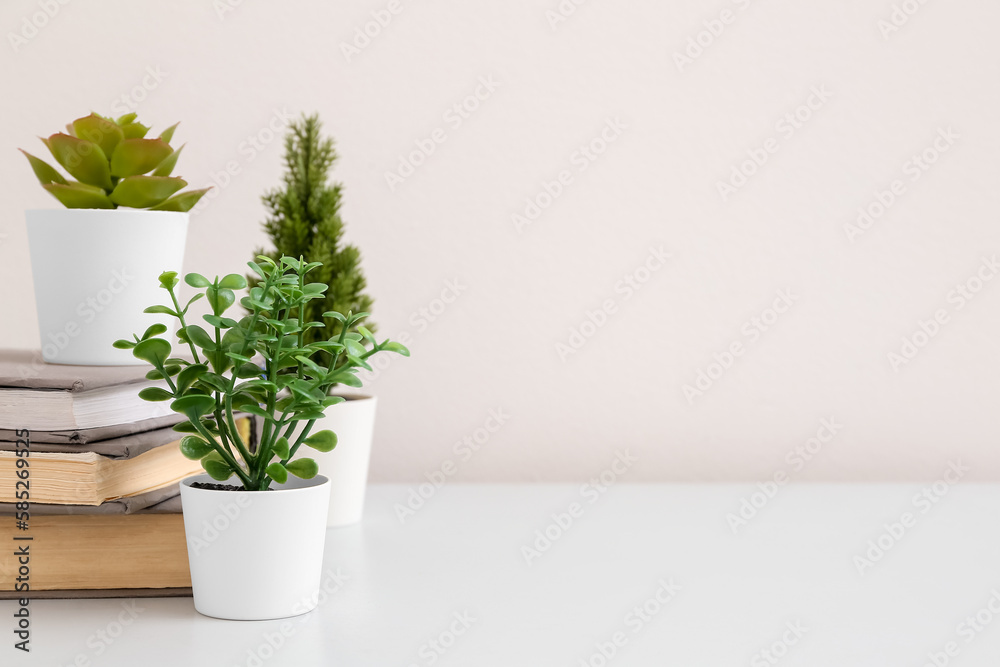 Artificial plants with books on table near light wall Stock Photo ...