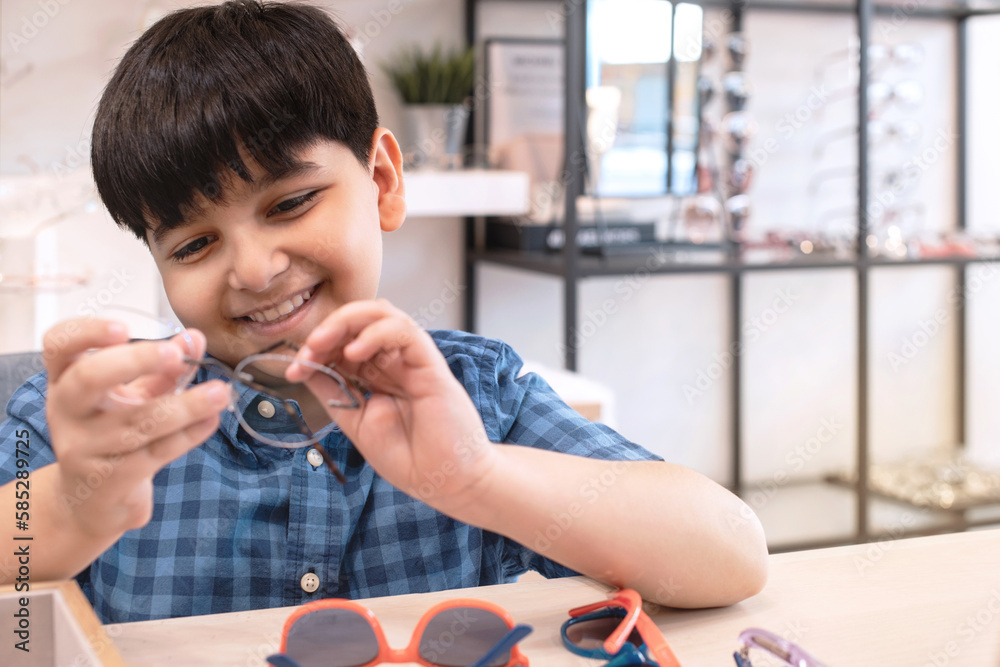 Indian child boy choosing glasses in optical store, holding glasses ...