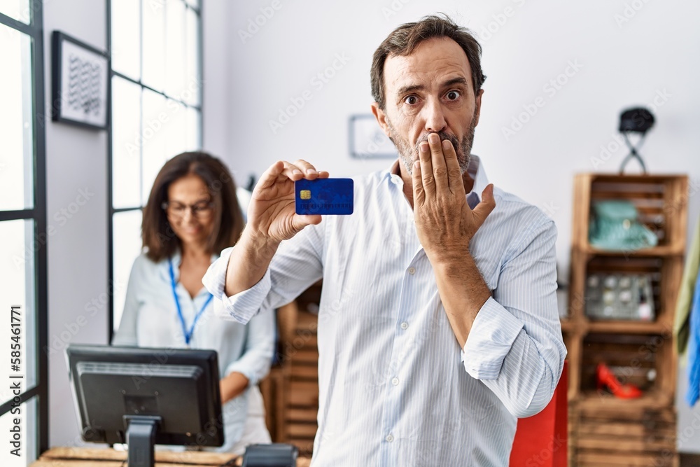 Hispanic man holding credit card at retail shop covering mouth with ...
