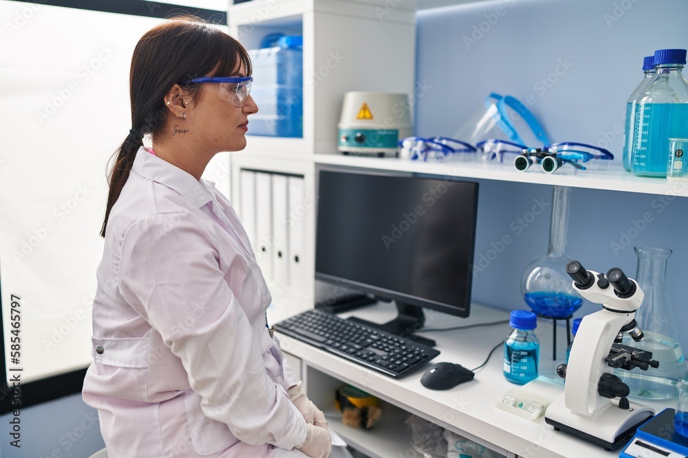 Young brunette woman working at scientist laboratory looking to side ...