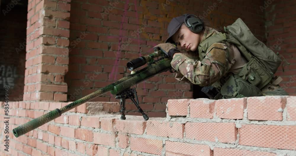 serious military woman in camouflage takes aim from the window of an ...