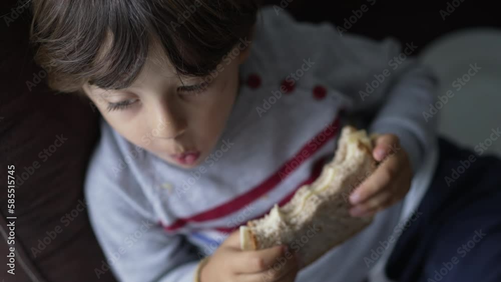 Kid taking a bite of sandwich laying on sofa. Child snacking carb food ...