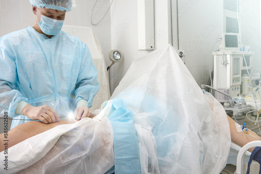 Patient lying behind screen operating table, experienced phlebologist ...